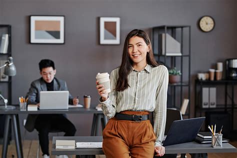 매력적인 젊은 아시아 여성의 초상화 들고 커피 의 컵 앉아 편안 하 게 사무실에서 미소 에 카메라 아시아인에 대한 스톡 사진 및 기타 이미지 Istock
