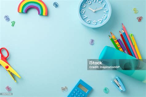 편지지 필통 펜 무지개 플라스틱 스테이플러 숫자 모양의 클립 가위 알람 시계와 같은 그림 용품이 배치된 책상의 평면도 파스텔 블루 배경 텍스트 또는 광고에 적합 0명에 대한