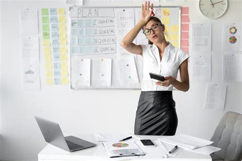 Female Accountant In Office With White Board Holding Calculator In