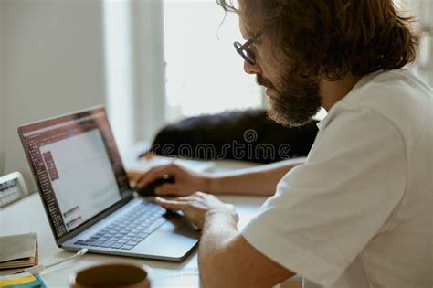 Close Up Of Focused Male Programmer Sitting At Desk And Working Laptop And Computer In Home