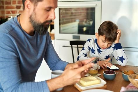 Father And Son Sitting With Mobile Phone While Breakfast Premium Photo