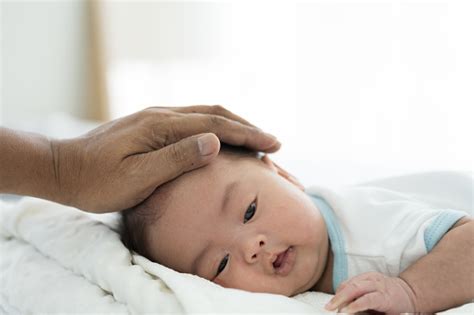 갓 태어난 아기가 침대에 엎드린 자세로 자고 있다 갓 태어난 아기나 유아가 하얀 침대에 누워 있고 아버지의 손은 조심스럽게 머리를 가리고 있다 가족 사랑 새로운 삶의 개념