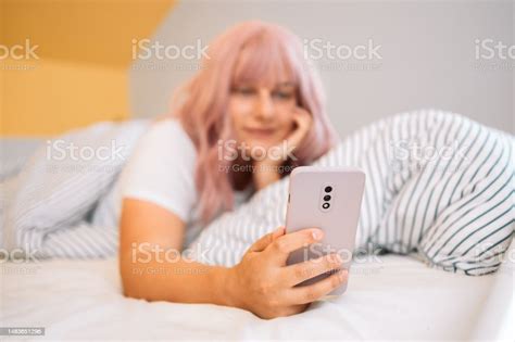 스마트폰 화면을 보고 좋은 소식을 듣고 집에서 침대에 누워 여유 공간을 확보한 편안한 여성 휴대 전화를 꽉 쥐고 주먹을 쥔 행복한 아가씨 갈색 머리에 대한 스톡 사진 및