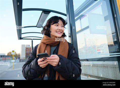 Cute Smiling Asian Girl Standing On Bus Stop Holding Smartphone