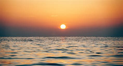 바다 표면 아래 큰 노란색 태양과 함께 밝은 일몰 해질녘 따뜻하고 잔잔한 파도가 이 아름다운 해변을 맞이합니다 빛 반사와 잔잔한 파도가 있는 물 표면 0명에 대한 스톡 사진