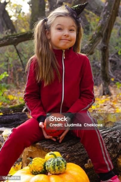 머리에 마녀의 모자를 쓰고 손에 작은 호박을 들고 있는 유럽 소녀 아이가 그루터기 위에 앉아 있다 노란 낙엽이있는 가을 숲 할로윈 10월에 대한 스톡 사진 및 기타 이미지