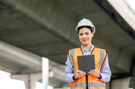 태블릿으로 건설을 원하는 아시아 엔지니어 노동자 여성 또는 건축가는 건설 현장에서 흰색 안전 헬멧을 착용합니다 고속도로 콘크리트 도로 현장에 서 있습니다 고속도로 교량의