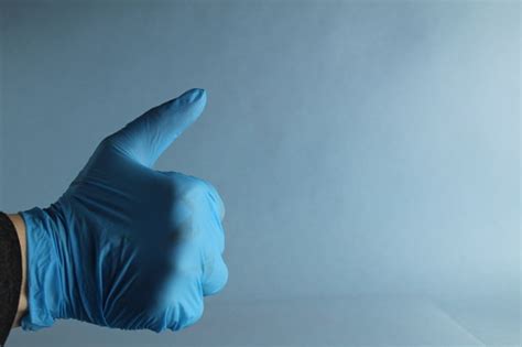 엄지손가락을 들고 실리콘 의료 장갑을 낀 한 여성의 손이 들어올렸다 흰색 격리 된 배경을 표시하는 손가락 그림입니다 코로나