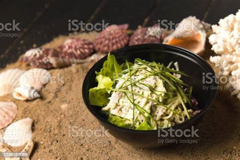 검은 플라스틱 음식 배달 그릇에 눈 게 고기 오이 채소를 곁들인 아시아 샐러드와 바다 껍질과 별이 모래 배경에 있습니다 거미게에 대한 스톡 사진 및 기타 이미지 Istock