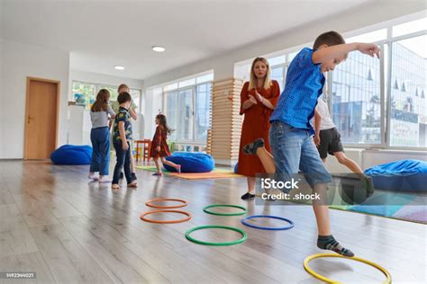 작은 보육원 아이들 교실에서 실내 바닥에 여성 교사와 함께 운동을하고 훌라 후프 서클을 뛰어 넘으면 바닥에서 추적됩니다 Mental Wellbeing에 대한 스톡 사진 및