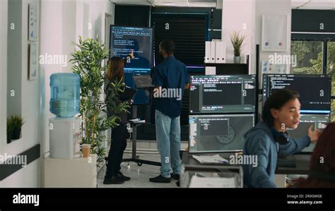 Diverse Team Of System Developers Analyzing Code On Big Tv Screen