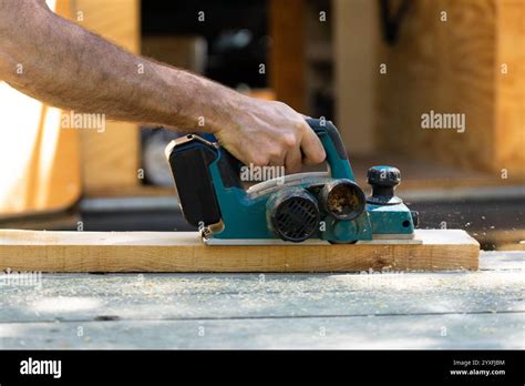 Carpenter Using Electric Planer Smoothing Wooden Plank In A Workshop