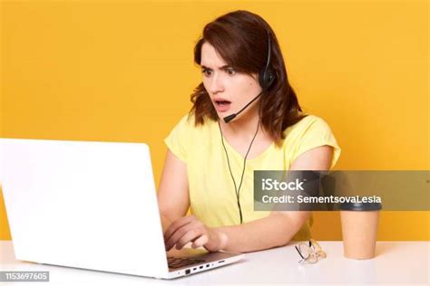 반 빼내야 사진 스튜디오에서 노란색 배경 위에 고립 된 Laptopon 화면을 보고 열린 입으로 앉아있는 신경 젊은 여자 운영자 어두운 머리 놀란 모델 사무실에서 작동