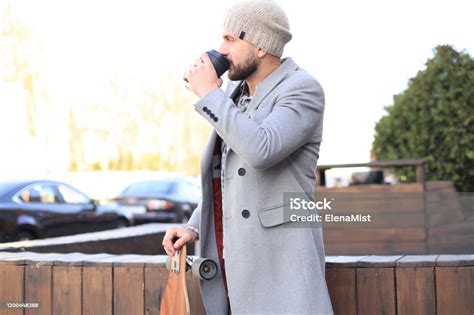 회색 코트와 모자를 입은 잘생긴 청년 휴식 롱 보드 마시는 커피와 함께 앉아 도시 스케이트 보드 개념입니다 거리에 대한 스톡 사진 및 기타 이미지 Istock