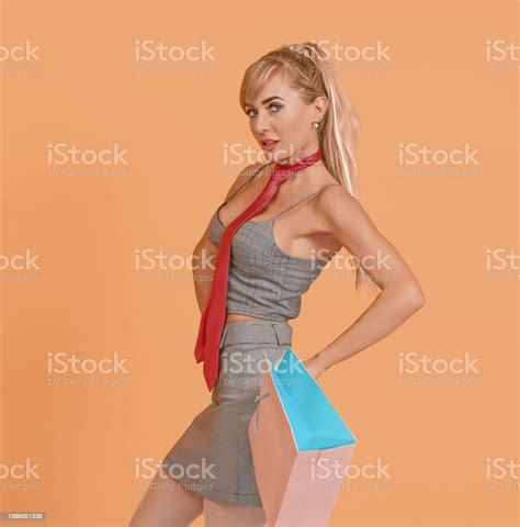 빨간 넥타이를 매고 회색 옷을 입은 젊은 금발 여성은 복사 공간이있는 조용한 배경에 종이 봉지를 들고 옆으로 서 있습니다 가방에 대한 스톡 사진 및 기타 이미지 Istock