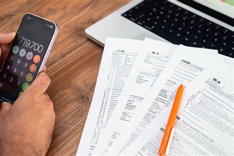 남자는 스마트 폰을 들고 세금 양식을 작성하여 연간 소득을보고하는 재무 계산을합니다 Brand Name Smart Phone에 대한 스톡 사진 및 기타 이미지 Brand