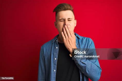 고립 된 빨간 배경 위에 서있는 데님 셔츠를 입은 젊은 잘생긴 남자는 손으로 입을 덮는 피곤한 하품 불안과 졸음 가리기에 대한 스톡 사진 및 기타 이미지 Istock