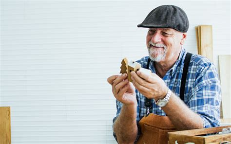 수석 노인 수염 종류 백인 남자 또는 목수 체크 셔츠를 입고 앞치마 아이들을위한 Diy 나무 장난감을 만들고 행복으로 미소 실내 집에서 혼자 앉아 은퇴 취미 개념 Diy에