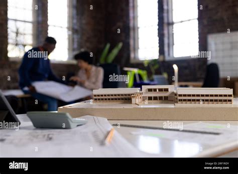 Building Model With Diverse Architects Discussing Blueprints In Background At Office Copy Space