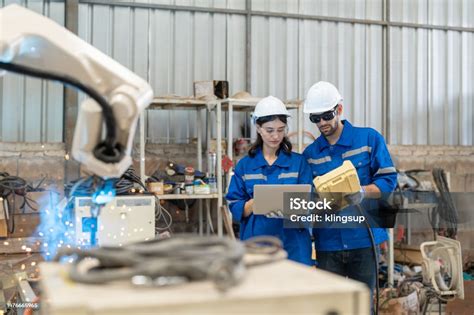 산업 공장에서 로봇 팔 용접기로 작업하는 노트북을 사용하는 남성과 여성 엔지니어 유니폼을 입은 기술자 자동화 로봇 팀이 로봇 팔 시스템을 설명합니다 공장 산업 건물에 대한