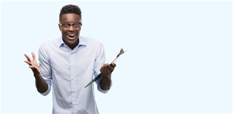 젊은 아프리카계 미국인 남자는 Clipboarad 매우 행복 하 고 흥분 상자 식 큰 웃음 소리는 승리를 축 하 하 고 손을 들고 검사 보기에 대한 스톡 사진 및 기타