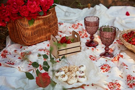 공원의 분홍색 장미 사이에 식탁보 마시멜로 딸기 체리 완두콩 및 와인 잔이있는 여성 핑크 여름 피크닉 낭만적 인 저녁 여행 및