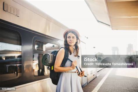 테마 철도 및 여행 여름에 드레스와 모자관광 고립 매트를위한 배낭 과 장비와 기차역 기차 배경에 서있는 이빨이 있는 미소를 가진 초상화 젊은 백인 여성 가방에 대한 스톡