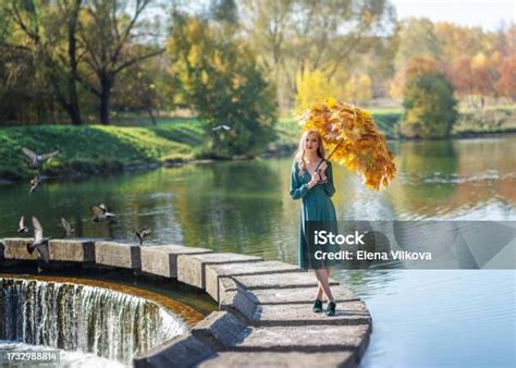 젊은 아름다운 여성이 호수를 배경으로 가을 공원에서 나뭇잎으로 만든 우산 아래에 서 있습니다 단풍 나무 잎의 우산 아래 공원에서 산책을하는 가을의 아름다운 여성 10월에