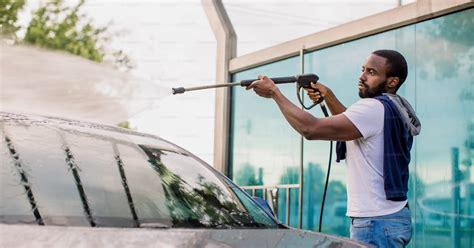 캐주얼 복장을 한 잘 생긴 아프리카 청년은 야외 셀프 세척 서비스에서 물 고압 호스로 빨간 차를 수동으로 씻습니다 세차 개념