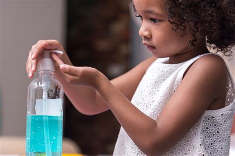 어린 아프리카 계 미국인 소녀 아이 넣어 알코올 젤 소독제 펌프 에 손 청소 얼굴에 얼굴 마스크를 착용 하기 전에 그의 손을 씻어 4 5세에 대한 스톡 사진 및 기타 이미지