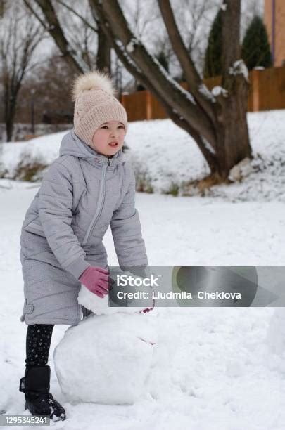 겨울 옷을 입은 소녀와 겨울 공원에서 눈으로 노는 모자 어린이는 겨울 방학 동안 밖에 있습니다 한 어린이가 눈덮인 눈사람을 만든다 6 7 살에 대한 스톡 사진 및 기타