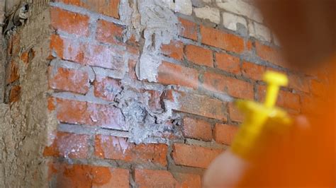 벽을 프라이밍 작업자가 스프레이 건으로 벽을 프라이머합니다 분쇄기 페인트에 더럽혀 보호 장갑에 손에 녹색 스프레이 총 배경에 흰색 프라이밍 벽입니다 건강관리와 의술에 대한