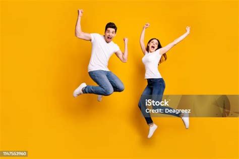 전체 길이 몸 크기 사진 펑키 그녀는 그를 그의 쌍 점프 높은 제기 주먹 소리 비명 외침 시끄러운 치 어 리더 축구 팬 캐주얼 청바지 데님 흰색 T 셔츠 고립 된 노란색