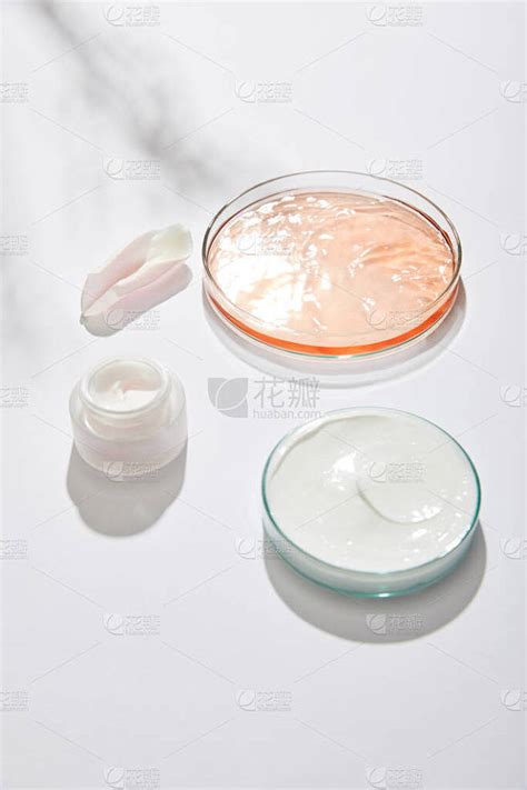 带有化妆品、液体和玫瑰叶的带阴影白色背景的实验室玻璃器皿
