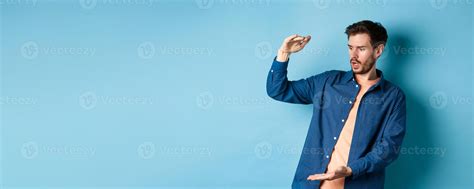 Shocked Young Man Looking At Empty Space And Showing Big Size Object