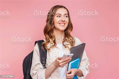 미소 짓고 멀리 바라보고 분홍색 배경 위에 고립 된 스마트 폰을 들고있는 학생 소녀 후면에 대한 스톡 사진 및 기타 이미지 후면 컷아웃 미소 Istock