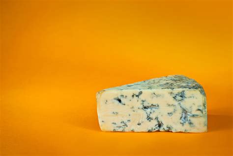 오렌지 배경에 치즈의 노란색 조각 곰팡이가 있는 삼각형 치즈가 가까이 있습니다 치즈 근처의 텍스트를 위한 공간과 여유 공간을 복사합니다 구멍에 대한 스톡 사진 및 기타