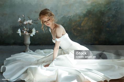 긴 흰색 드레스에 바닥에 앉아 아름다운 날씬한 금발의 소녀 손에 꽃 그녀의 얼굴에 베일과 초상화 여자 완벽한 헤어 스타일과 화장품 신부 새로운 컬렉션 웨딩 드레스 드레스에