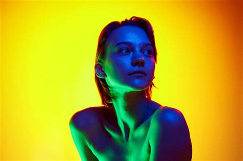 그라데이션 스튜디오 배경에 대해 네온 불빛에서 멀리 바라보고 포즈를 취하는 벌거 벗은 어깨를 가진 젊은 여자의 초상화 잘 관리된