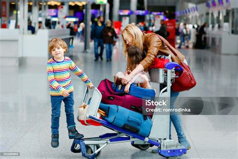공항에서 두 어린 아이 소년과 소녀 형제 자매와 어머니 어린이 가족 여행 비행기로 휴가를 가고 비행기를 타기 위해 터미널에서 여성이 밀어내는 여행 가방을 들고 트롤리를