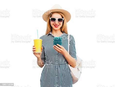 스마트 폰과 밀짚 모자를 쓴 주스 컵 흰색 배경에 고립 된 배낭으로 웃는 젊은 여성의 여름 초상화 스마트폰에 대한 스톡 사진 및