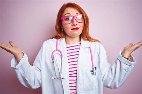 고립 된 분홍색 배경 에 서 청진기를 사용하여 젊은 빨간 머리 의사 여성은 팔과 손을 들고 단서와 혼란스러운 표정 의심 개념 감정에 대한 스톡 사진 및 기타 이미지 Istock