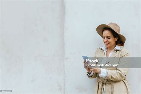 거리에서 야외에 서있는 동안 휴대 전화를 사용하여 따뜻한 코트와 모자를 쓴 여성 Brand Name Smart Phone에 대한 스톡 사진 및 기타 이미지 Brand