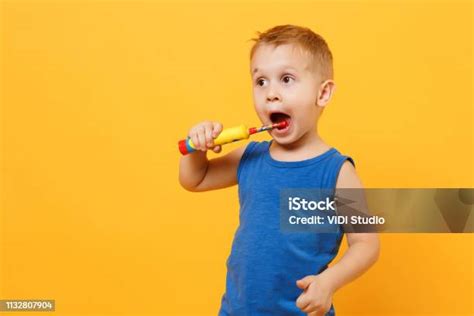파란 셔츠에 있는 아이 소년 34 세는 밝은 노란 주황색 벽 배경 아이 들 스튜디오 초상화에 고립 된 칫 솔을 가진 그의 이빨을 닦 습니다 사람들 어린 시절 라이프 스타일