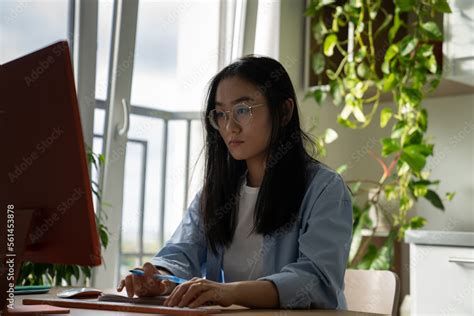 Focused Asian Woman It Developer Wearing Glasses Writing Code While Working Remotely From Home