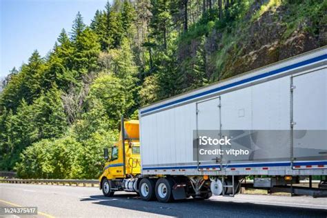 산 위의 숲이있는 멋진 고속도로 도로에서 마른 밴 세미 트레일러로 운전하는 지붕 스포일러가있는 데이 택시 노란색 큰 리그 세미 트럭 0명에 대한 스톡 사진 및 기타 이미지