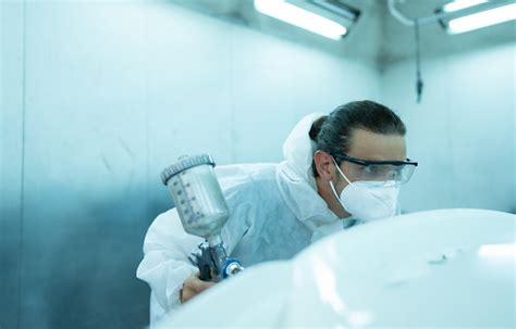 자동차 스프레이 룸의 자동차 정비사 안료가 완전하고 아름답고 자동차의 원래 색상과 조화를 이루는 자동차 앞 범퍼에 뿌려진 페인트를 검사합니다 가리기에 대한 스톡 사진 및