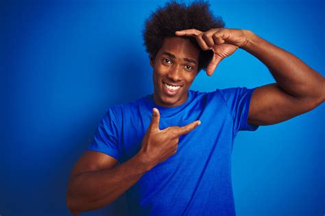 행복한 얼굴로 손과 손가락으로 프레임을 만드는 고립 된 파란색 배경 위에 서있는 티셔츠를 입은 아프리카 계 미국인 남자 창의력과 사진 개념 T 셔츠에 대한 스톡 사진 및