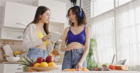 십대 아시아 여성은 음악에 헤드폰을 착용하고 과일 칼을 사용하여 야채 샐러드를 만드는 것은 친구들과 함께 부엌에 있습니다 요리에서 행복하게 함께 사는 레크리에이션 인생에서
