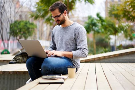 커피와 함께 캠퍼스 내부에 앉아서 고속 4 G 인터넷 연결을 사용 하 여 현대 노트북 컴퓨터의 키보드에 텍스트 메시지를 입력 광 안경에 긍정적인 수염된 Hipster 남자